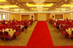 Uma sala de banquetes com mesas redondas, tapete vermelho e lustres.