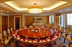 Uma sala de conferências com uma mesa redonda, cadeiras e um lustre.