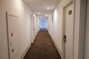 Corredor de hotel com portas em ambos os lados, piso coberto de carpete e parede em tom claro.