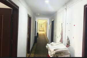 Corredor de hotel com portas em ambos os lados, piso coberto de carpete e uma pilha de toalhas dobradas ao fundo.