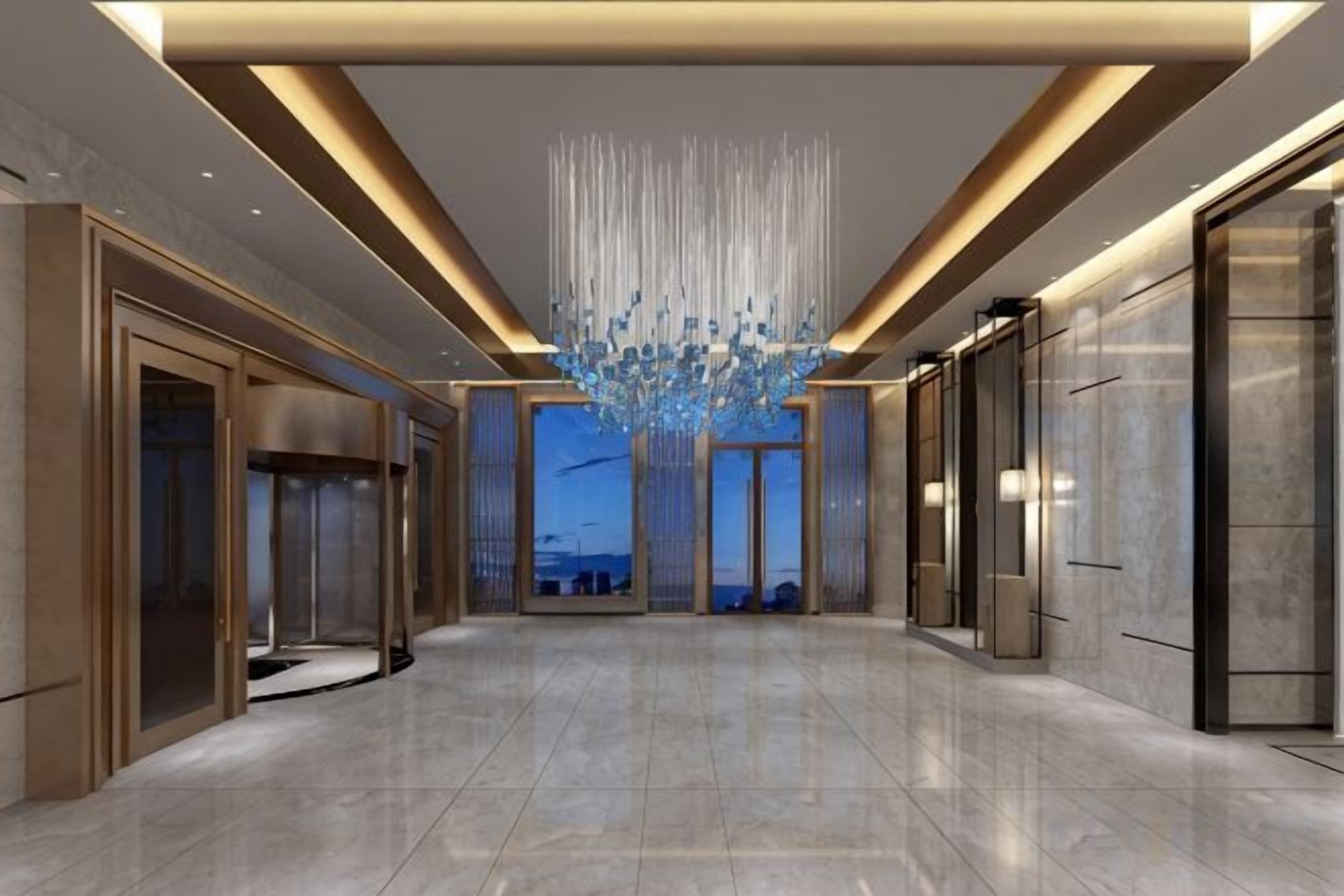 Um hall amplo com um lustre moderno, elevadores e vista através das portas de vidro.