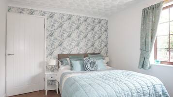 Quarto com cama, mesa de cabeceira, janela com cortinas e porta.