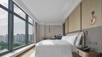 Quarto de hotel moderno com uma janela grande, uma cama, uma mesa de cabeceira com telefone e uma escrivaninha com cadeira.