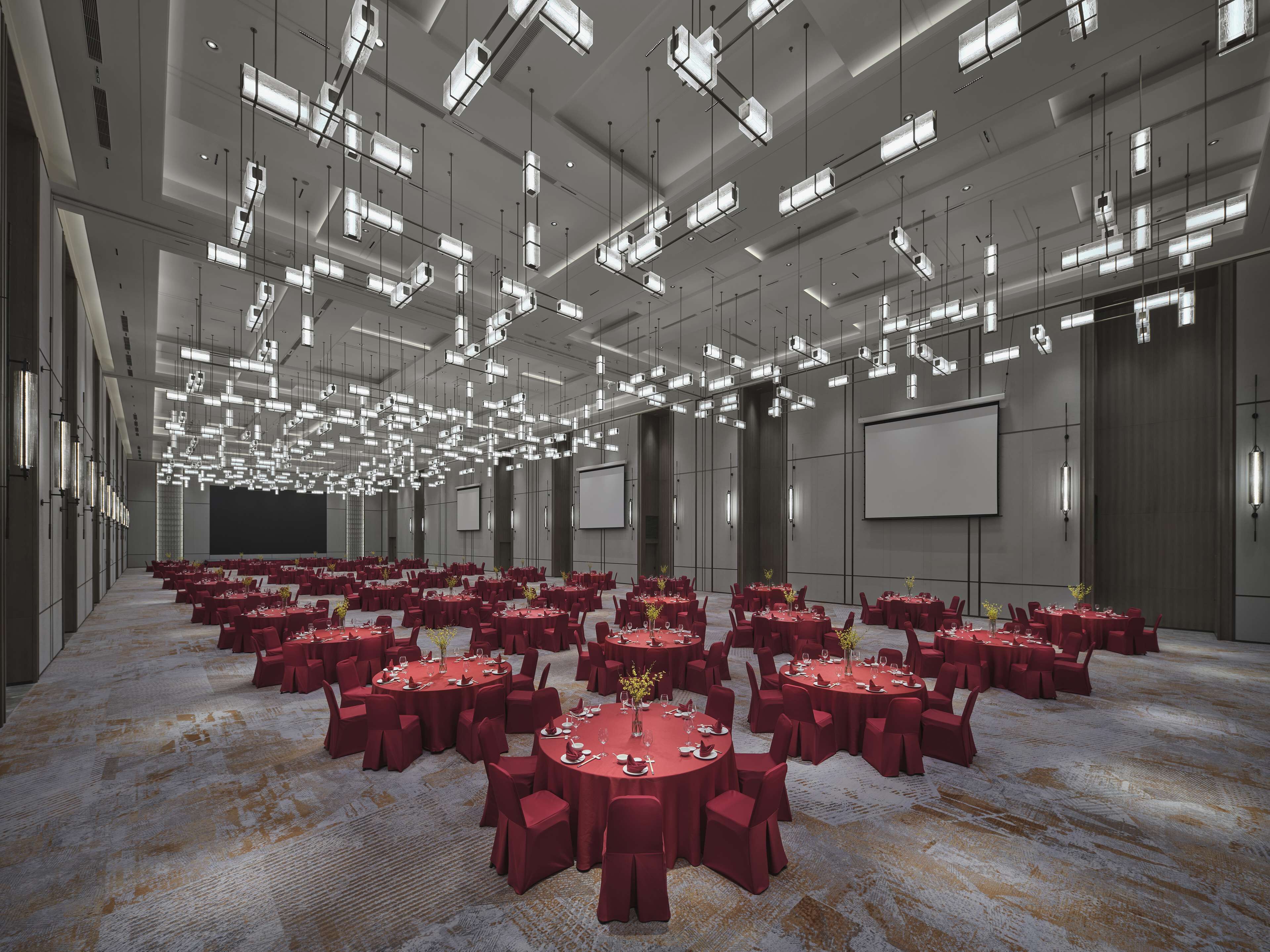 Uma sala de conferências ampla com várias mesas e cadeiras, uma tela grande e luminárias modernas.