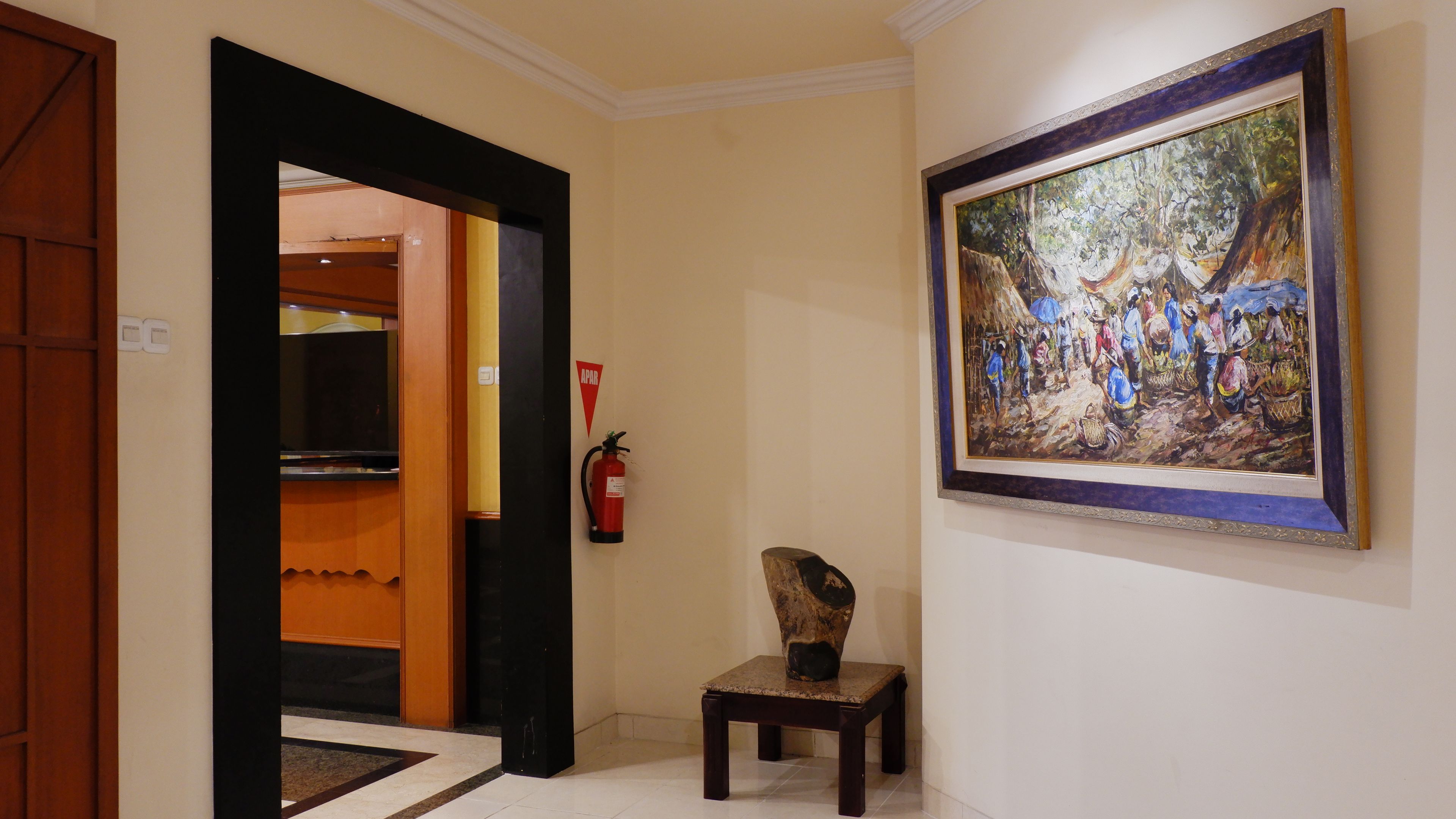 Um corredor com um quadro emoldurado, um extintor de incêndio e uma cadeira.