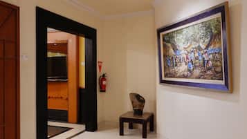 Um corredor com um quadro emoldurado, um extintor de incêndio e uma cadeira.