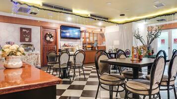 Um restaurante com chão xadrez, balcão de madeira e televisão na parede.
