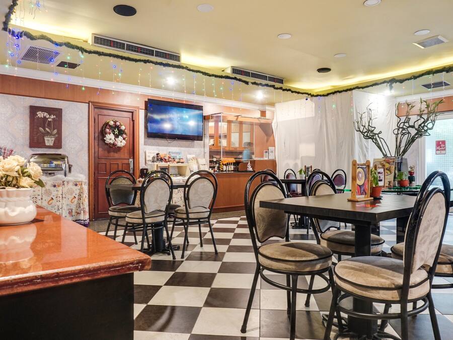 Um restaurante com chão xadrez, balcão de madeira e televisão na parede.