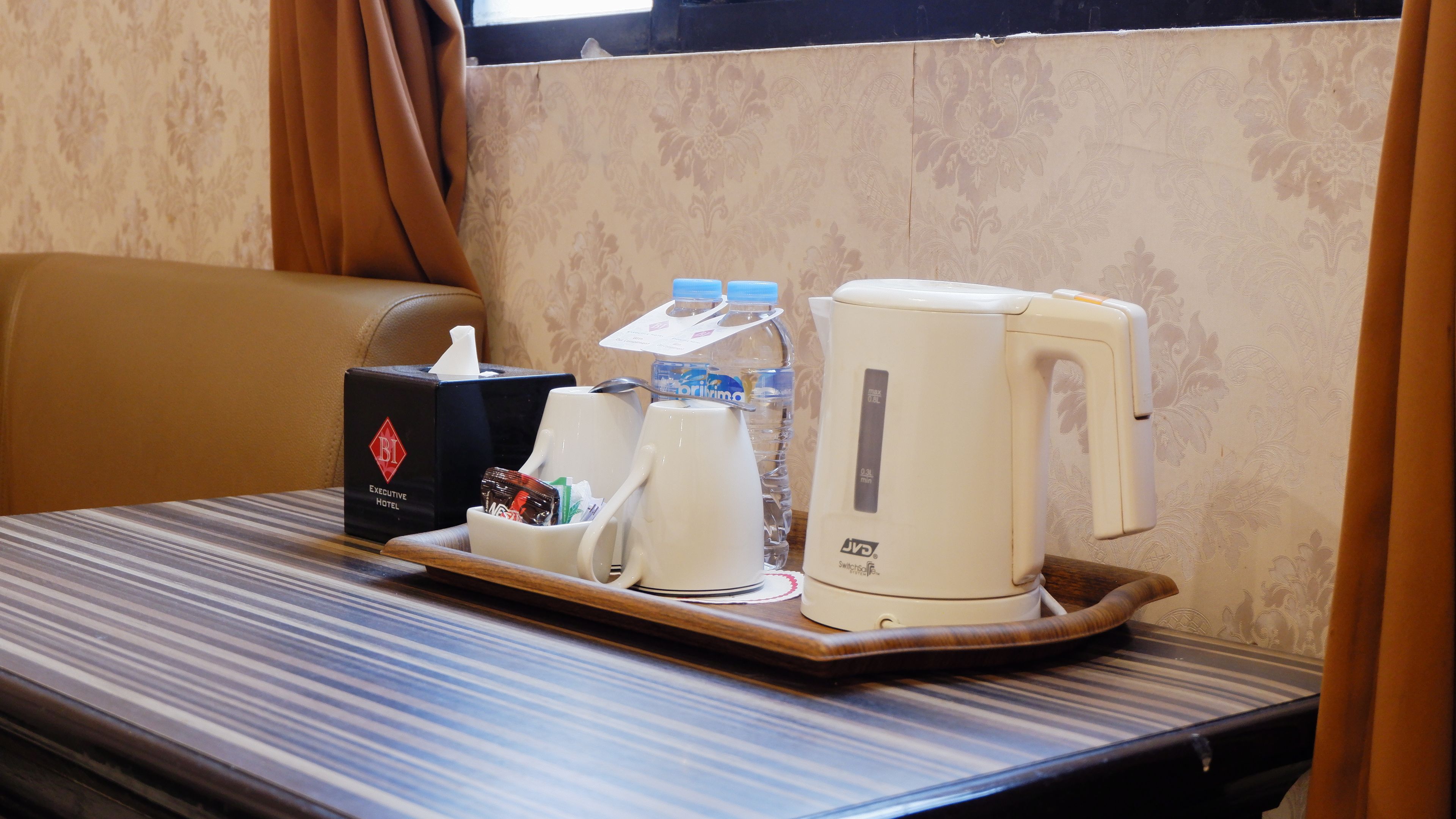 Uma bandeja com um estojo de lenços, uma garrafa de água, uma caneca e uma cafeteira em cima de uma mesa.