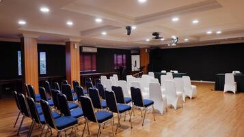 Uma sala de conferências com fileiras de cadeiras, um palco com um pódio e um projetor.