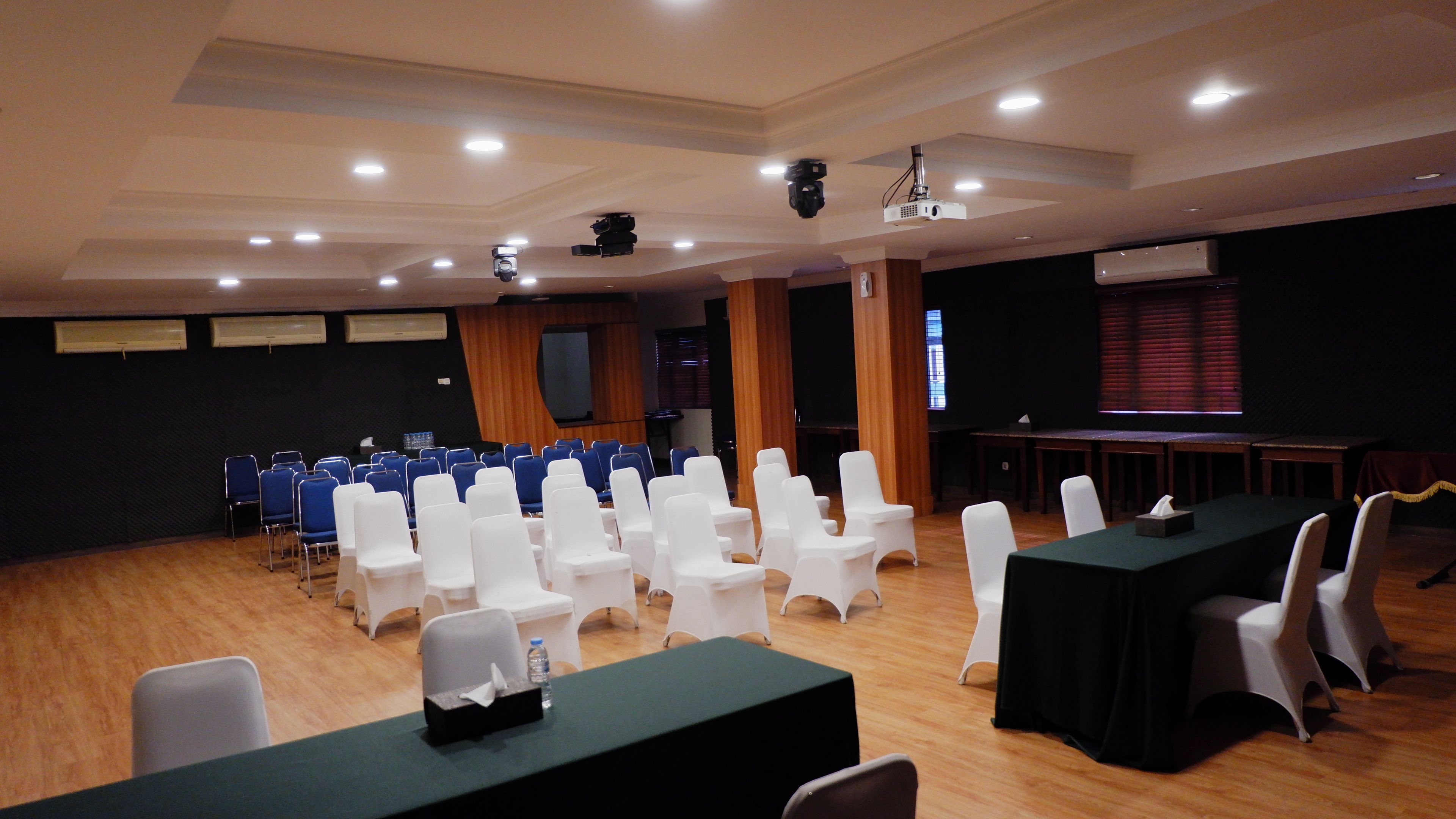 Uma sala de conferências com fileiras de cadeiras, mesas e um palco com um projetor.