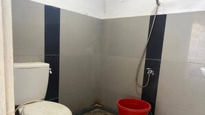 Casa de banho pequena, com azulejos, um chuveiro, um sanita e um balde vermelho.