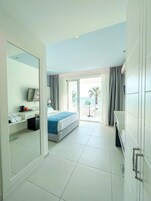 Quarto de hotel com cama, escrivaninha, espelho e vista para o mar.