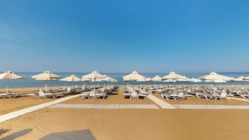 Uma praia com fileiras de espreguiçadeiras e guarda-sóis.