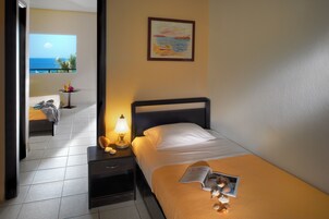 Quarto de hotel com uma cama, mesa de cabeceira, abajur, quadro emoldurado e vista para o oceano.