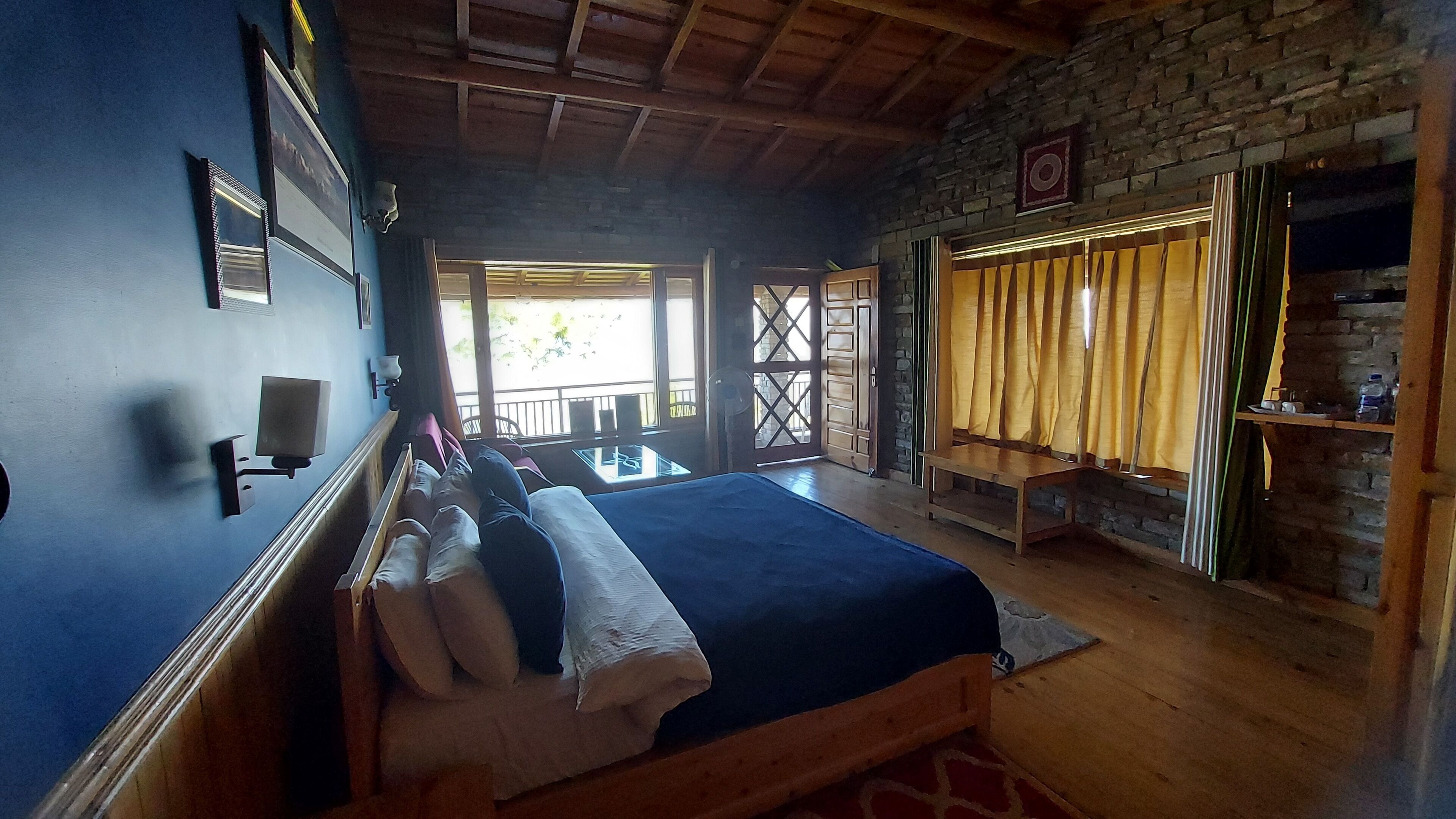Quarto com cama, ventilador, janela com cortinas e parede de pedra.