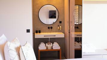 Quarto de hotel com um espelho redondo, um banco de madeira com toalhas e um banheiro moderno com um espelho grande.
