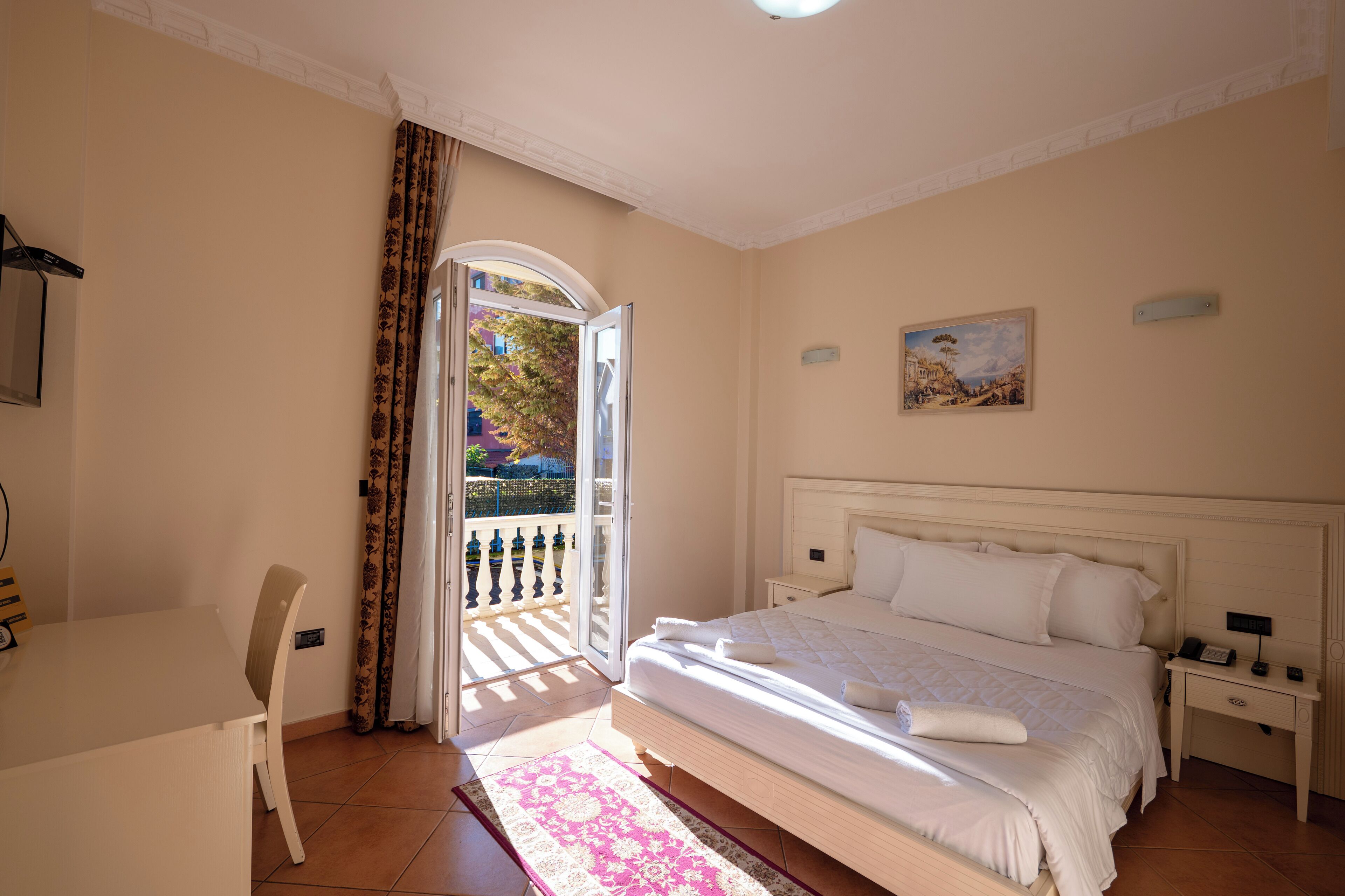 Quarto com cama, mesa de cabeceira, cadeira e porta aberta para uma varanda.