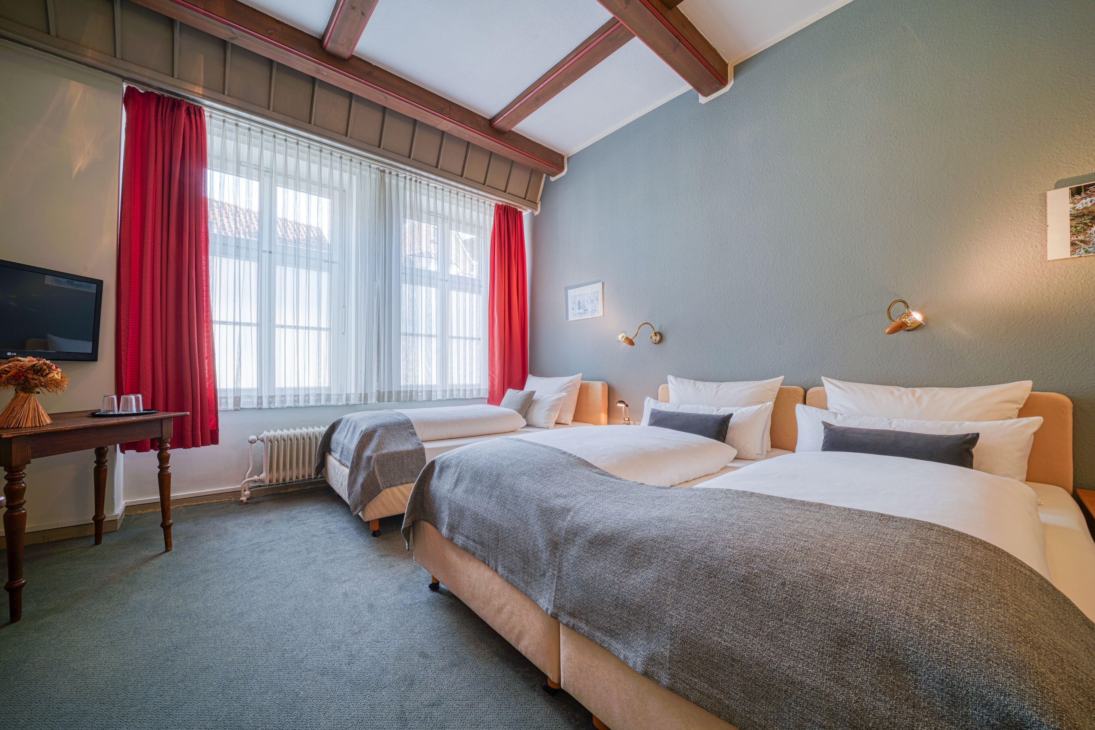 Quarto de hotel com duas camas, uma escrivaninha, um radiador e uma televisão.