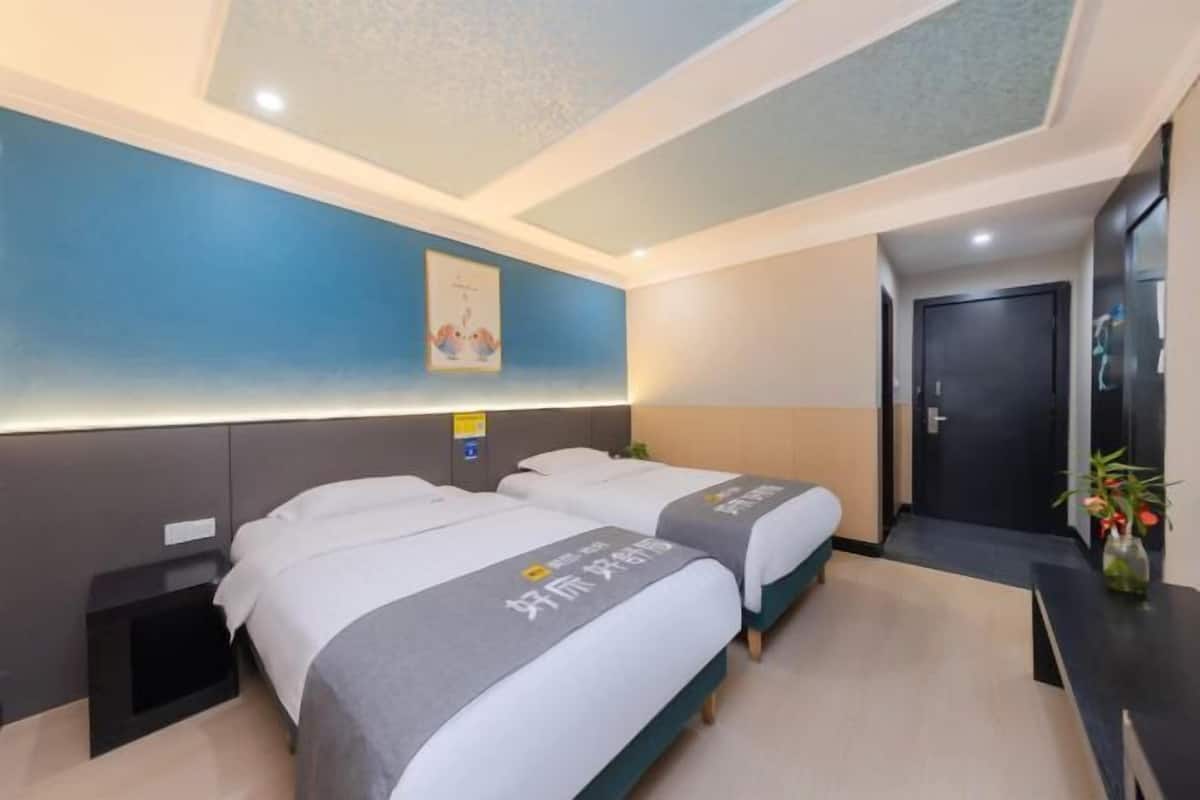 Quarto de hotel com duas camas, uma mesa de cabeceira, uma escrivaninha e uma obra de arte na parede.