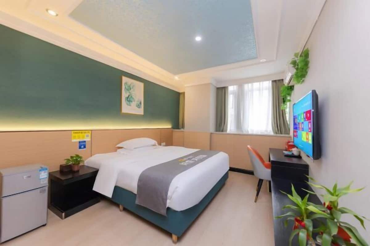 Quarto de hotel com cama, escrivaninha, cadeira, televisão e uma pequena mesa com uma planta.