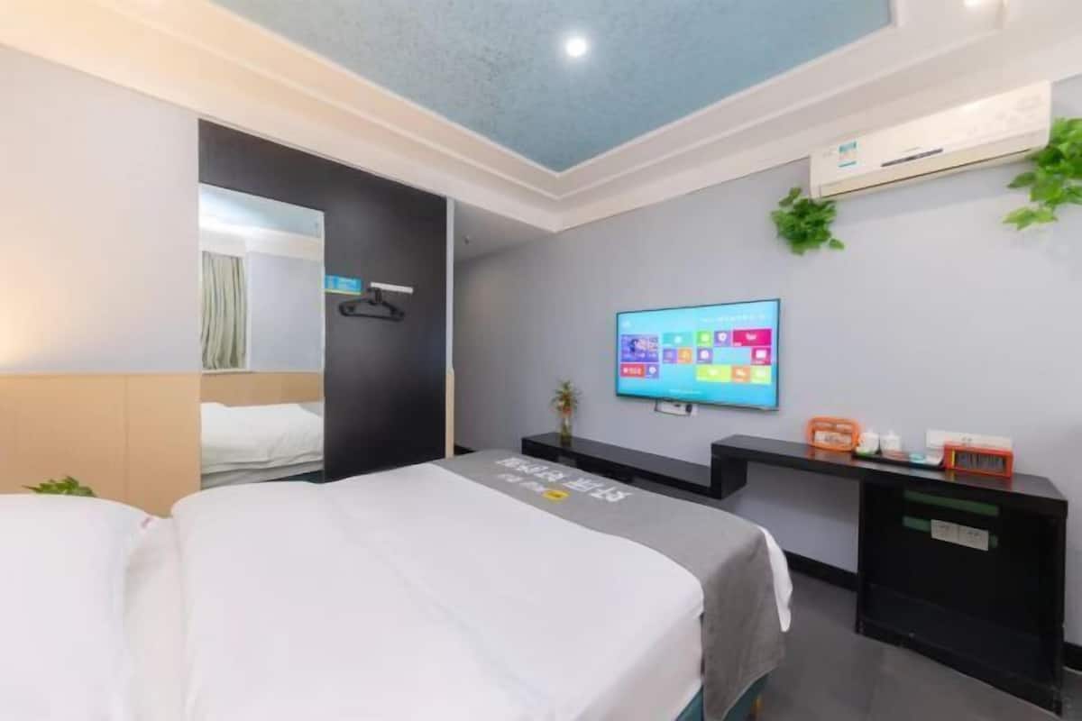 Quarto de hotel com uma cama, uma escrivaninha, uma televisão e um ar condicionado.
