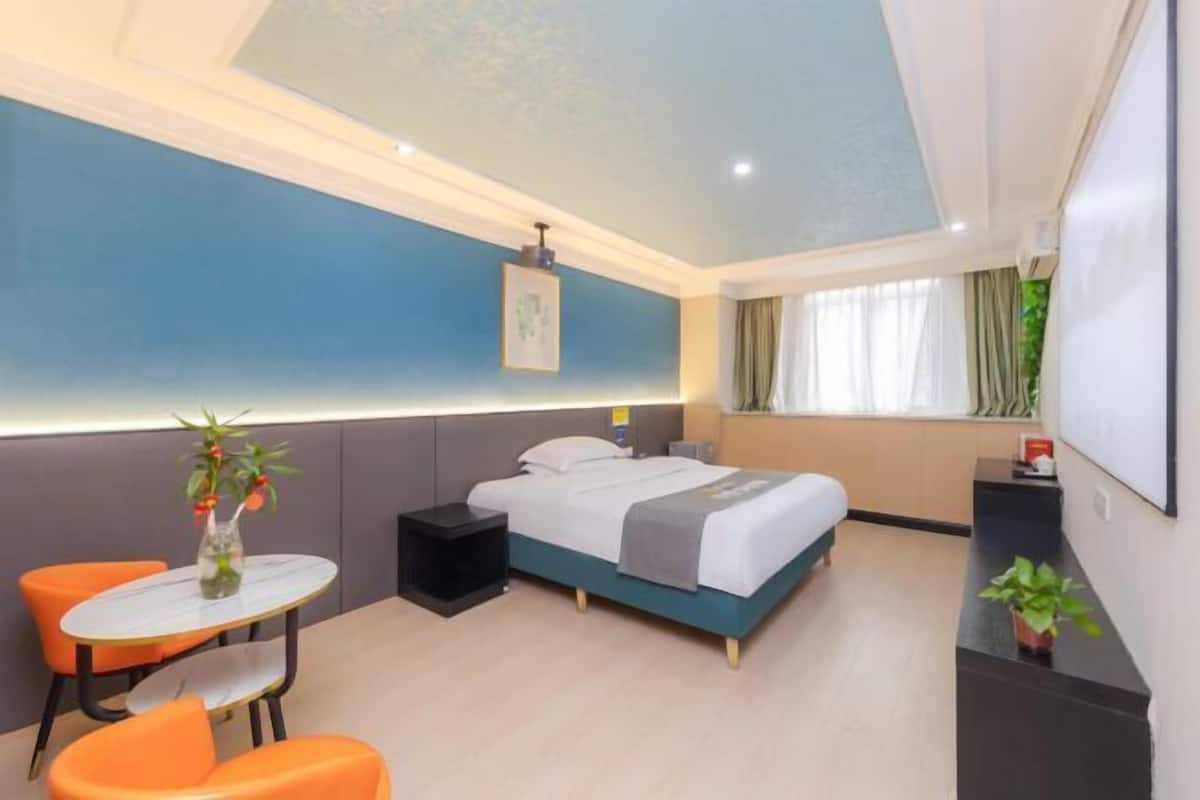 Quarto de hotel moderno com cama, escrivaninha, cadeira, mesa pequena com um vaso e janela com cortinas.