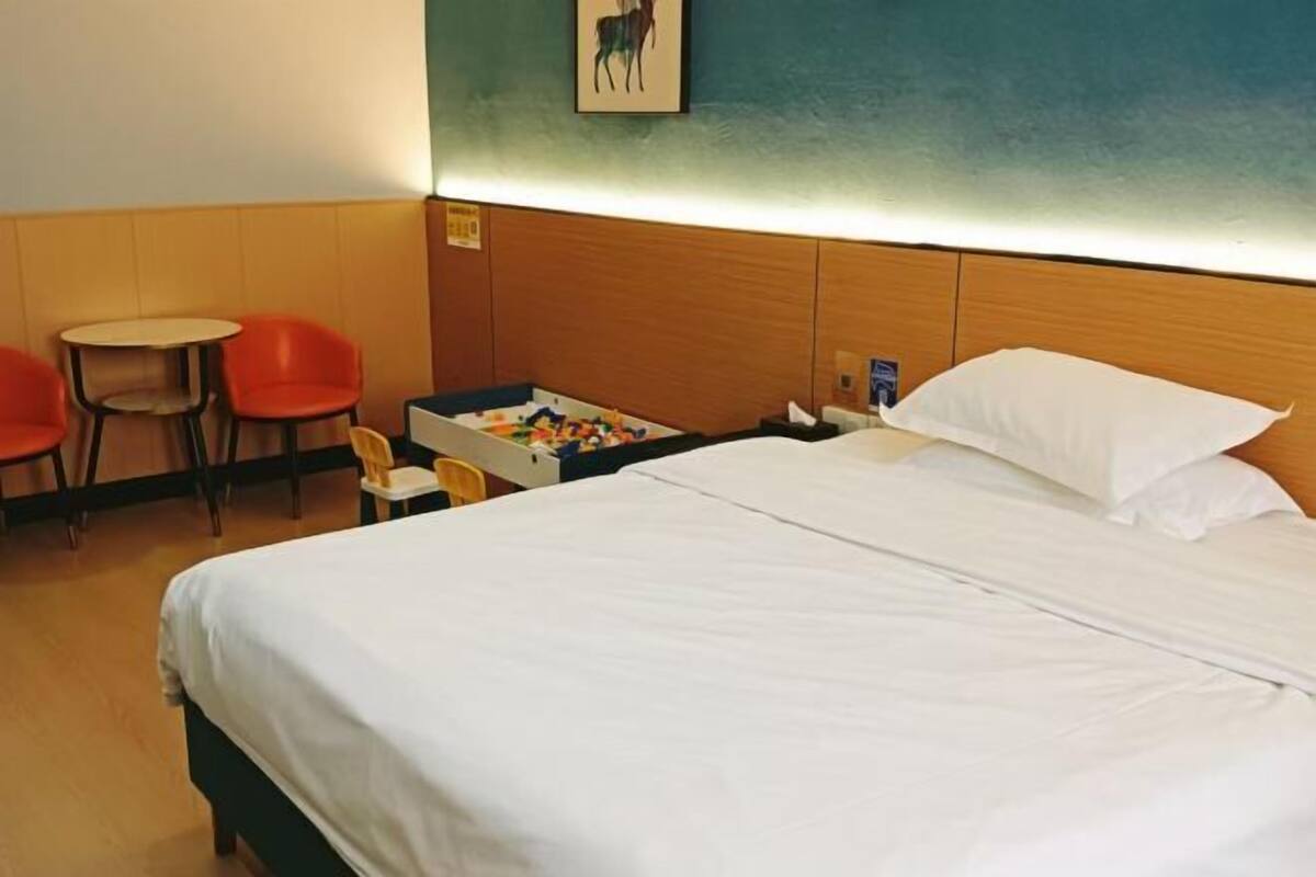 Quarto de hotel com uma cama, uma mesinha, duas cadeiras e uma mesa de cabeceira com abajur.