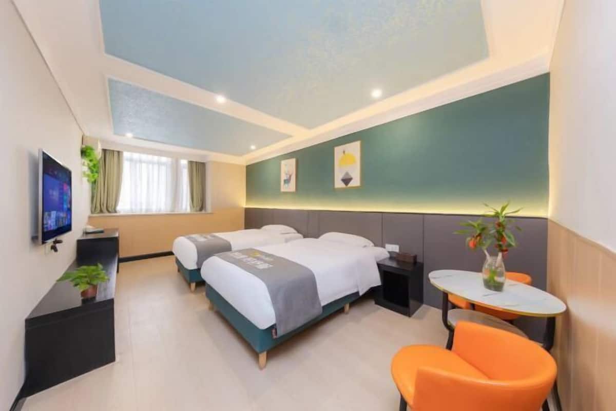 Quarto de hotel com duas camas, uma escrivaninha, uma cadeira, uma televisão e uma mesinha com um vaso.