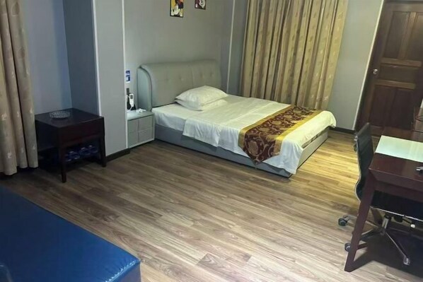 Quarto de hotel com uma cama, uma escrivaninha, uma cadeira e uma mesinha.