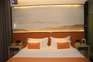 Quarto de hotel com uma cama grande, duas mesinhas de cabeceira, um telefone fixado na parede e uma mesinha de cabeceira com cafeteira.