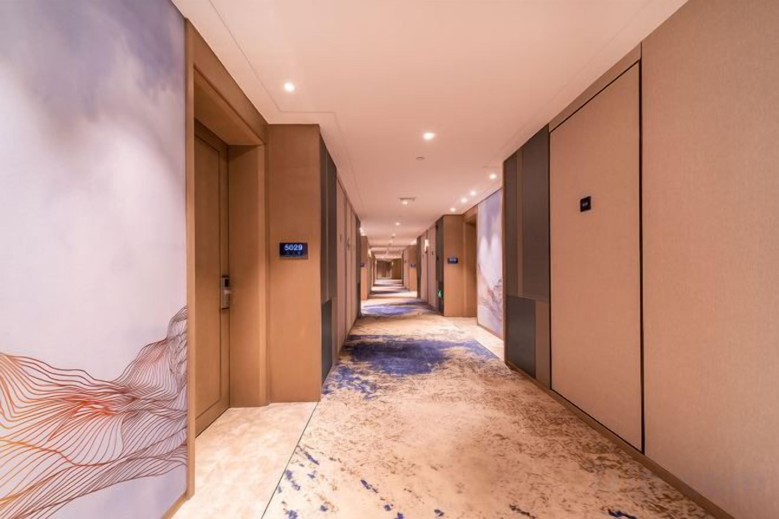 Um corredor de hotel com carpete no chão, portas em ambos os lados e uma placa com número na parede.