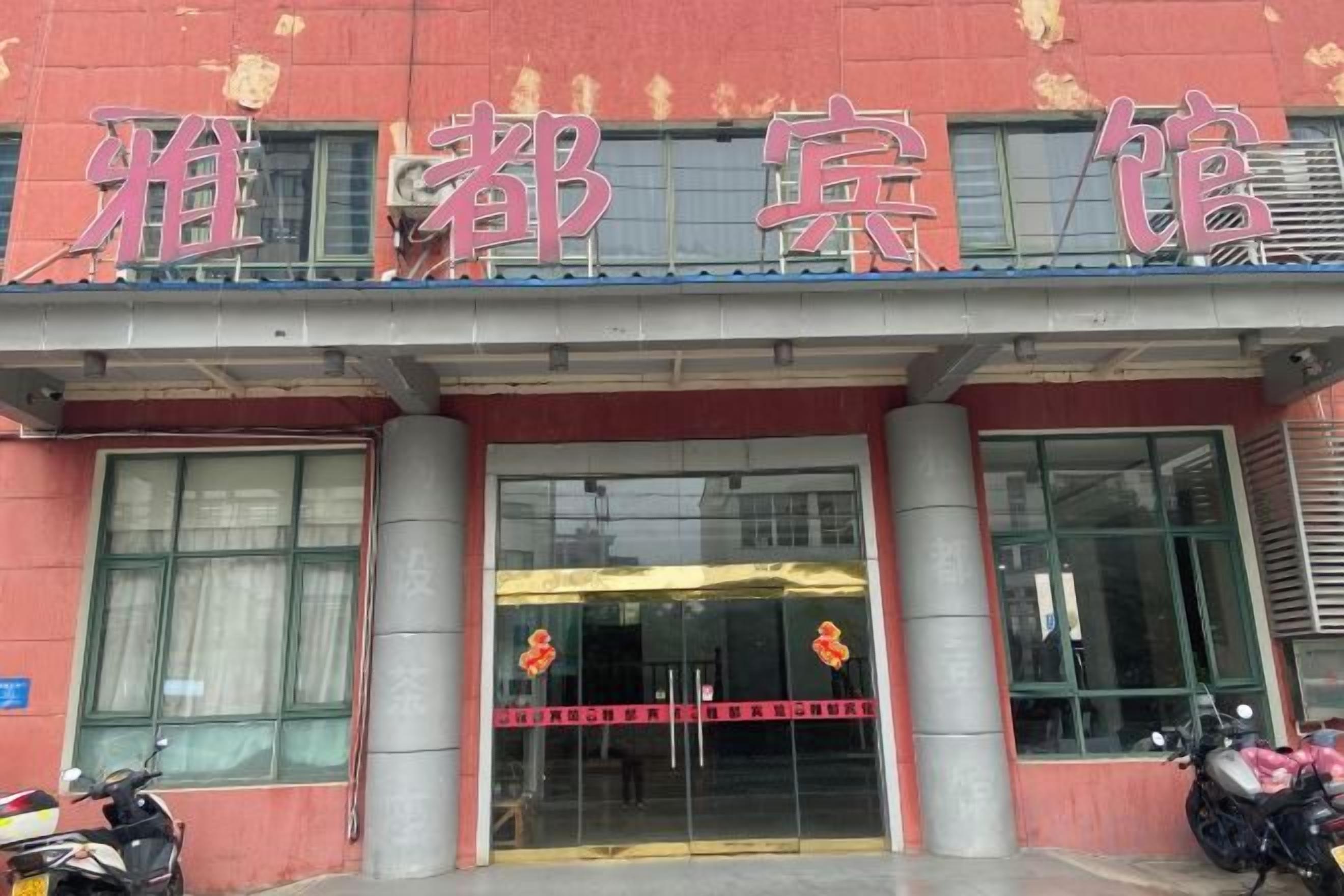 Um edifício com fachada vermelha e uma placa com caracteres chineses. Possui duas grandes janelas no andar térreo e uma porta com painel de vidro.