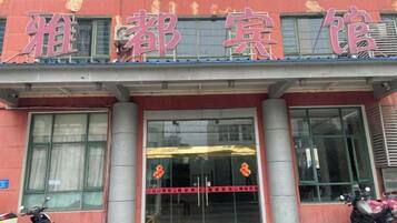 Um edifício com fachada vermelha e uma placa com caracteres chineses. Possui duas grandes janelas no andar térreo e uma porta com painel de vidro.