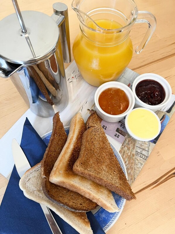 Uma bandeja de café da manhã com torradas, um jarro de suco de laranja e potes pequenos de geleia e manteiga.