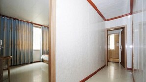 Um corredor com piso de madeira, porta de madeira e janela com cortinas azuis.