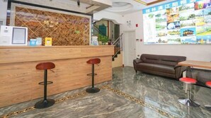 Uma área de recepção com balcão de madeira, dois bancos altos vermelhos, um sofá de couro marrom e uma parede com colagem de imagens.