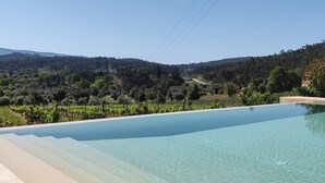 Piscina azul límpida com vista para um vinhedo e colinas ao fundo.