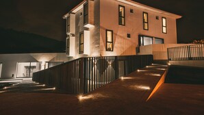 Um edifício moderno de vários andares com uma escadaria que leva à entrada, iluminado por luzes no chão.