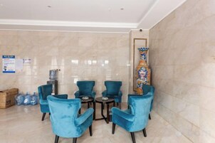Um saguão com cadeiras azuis, uma mesa pequena e um pilar decorativo.