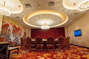 Uma sala de conferências com mesa redonda, cadeiras, lustre, pintura na parede e televisão.