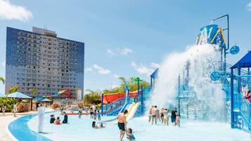 Um parque aquático com um edifício grande ao fundo, um toboágua e pessoas aproveitando as instalações.