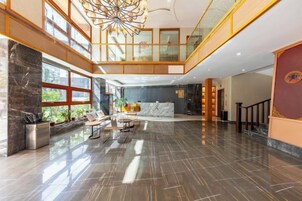 Um hall espaçoso com teto alto, balcão de recepção em mármore e área de estar com cadeiras e mesas.