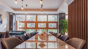 Sala de conferências com uma mesa comprida, várias cadeiras e uma janela grande com vista para áreas verdes.