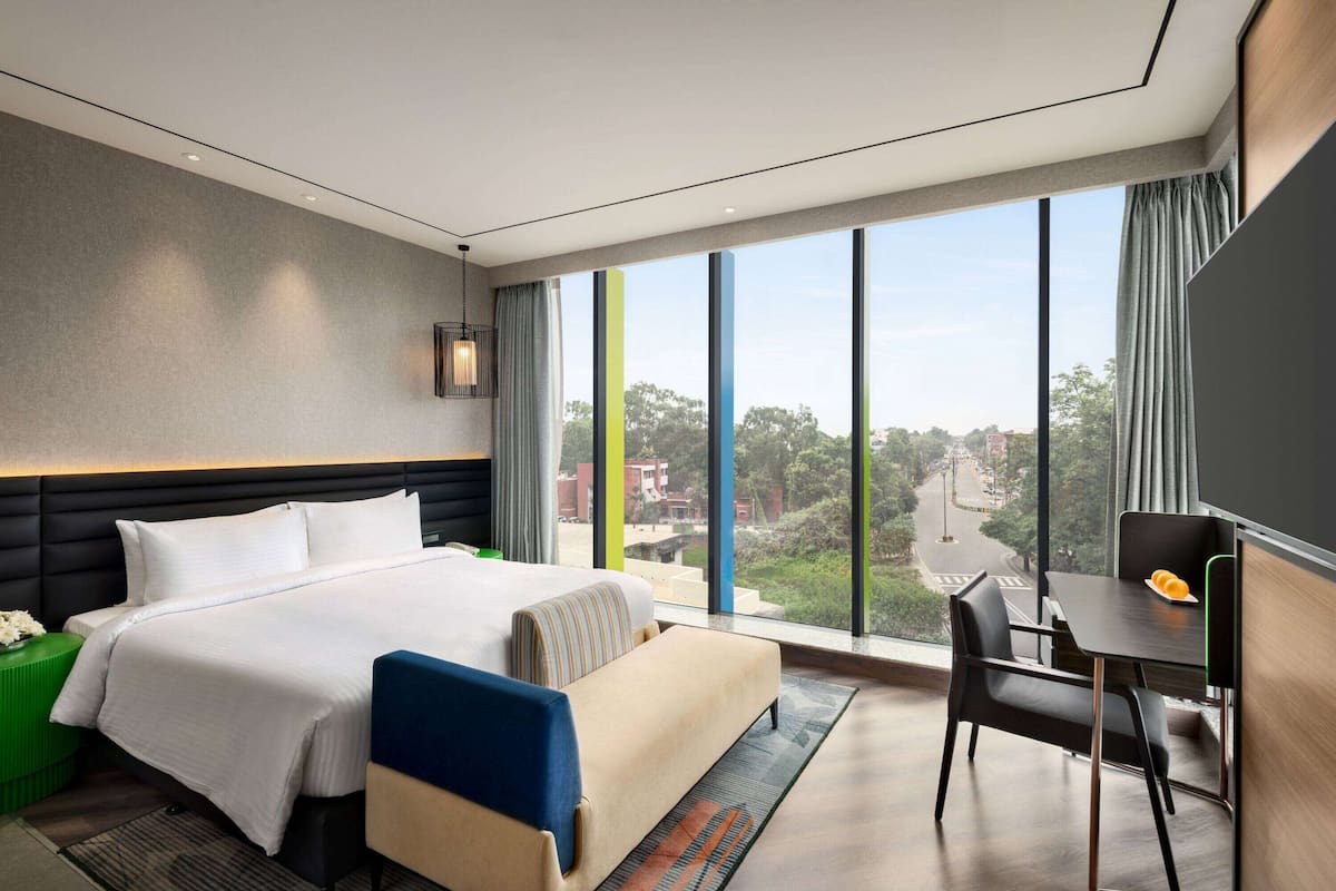Quarto de hotel moderno com uma cama grande, uma escrivaninha e vista para a cidade.