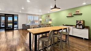 Cozinha moderna com mesa e cadeiras de madeira, uma máquina de café e vista pela porta de vidro.