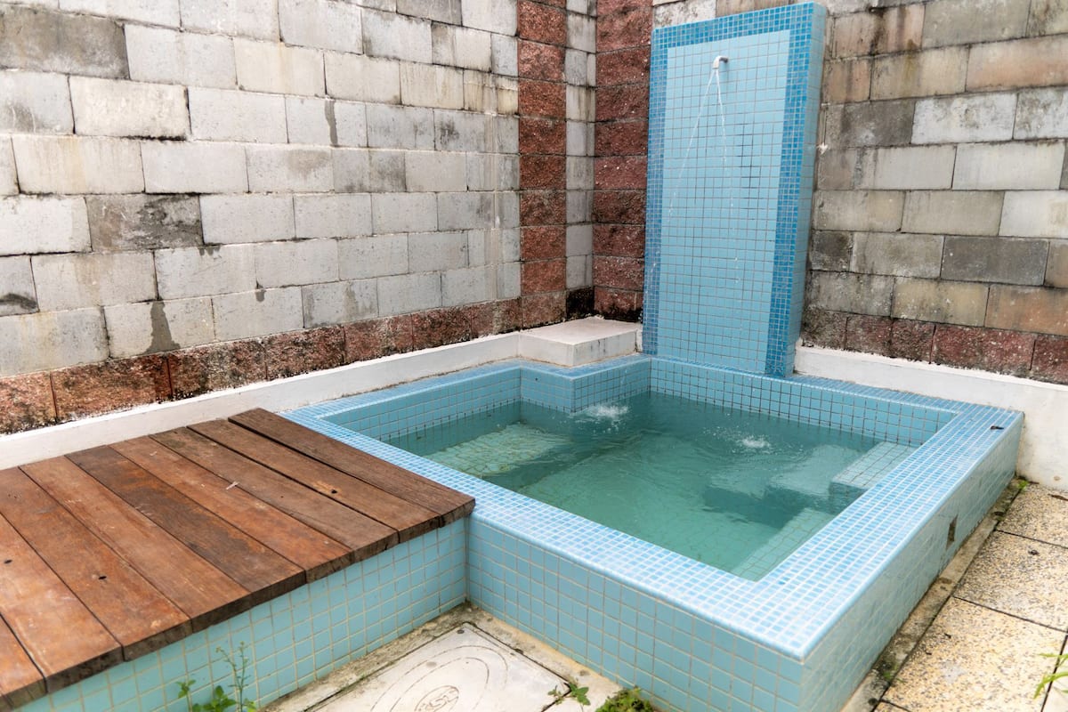 Uma banheira de hidromassagem retangular com azulejos de mosaico azuis, cercada por uma parede de tijolos e um deck de madeira.