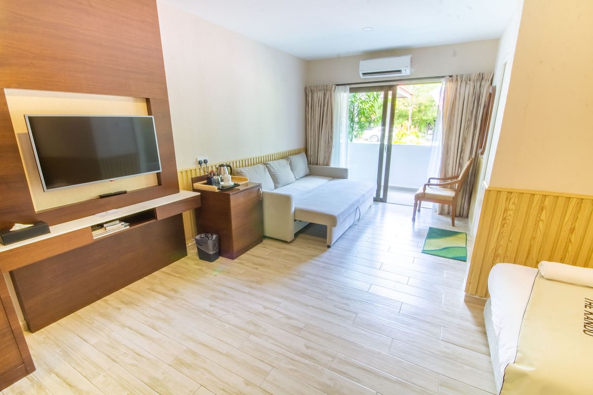 Quarto de hotel com televisão de tela plana, cama, sofá, poltrona e uma pequena mesa.