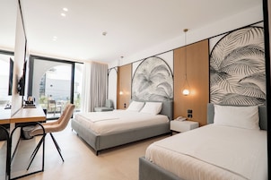 Quarto de hotel moderno com duas camas, uma escrivaninha, uma cadeira e uma janela grande.