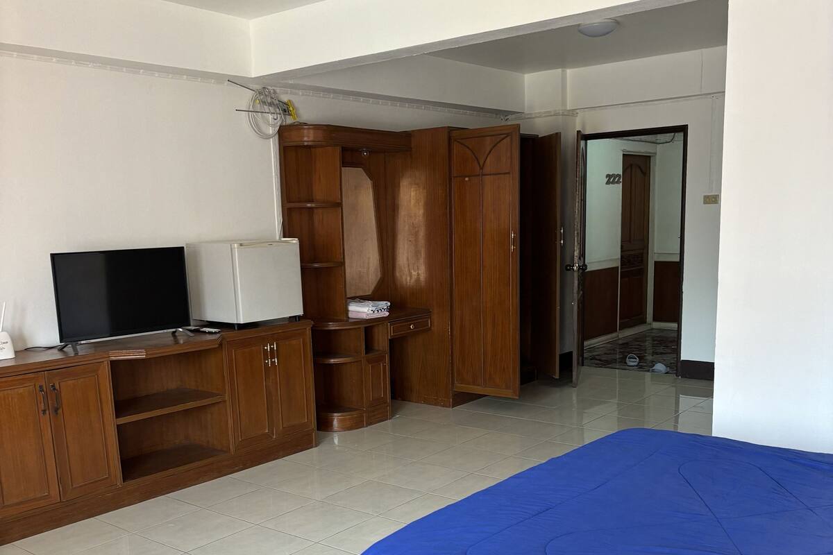 Quarto com cama, televisão, guarda-roupa e um pequeno frigorífico.